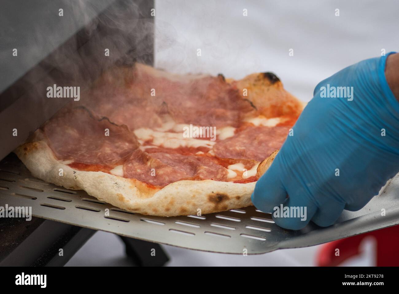 Hand with plastic glove cooking or baking hot pizza with tomato sauce ...