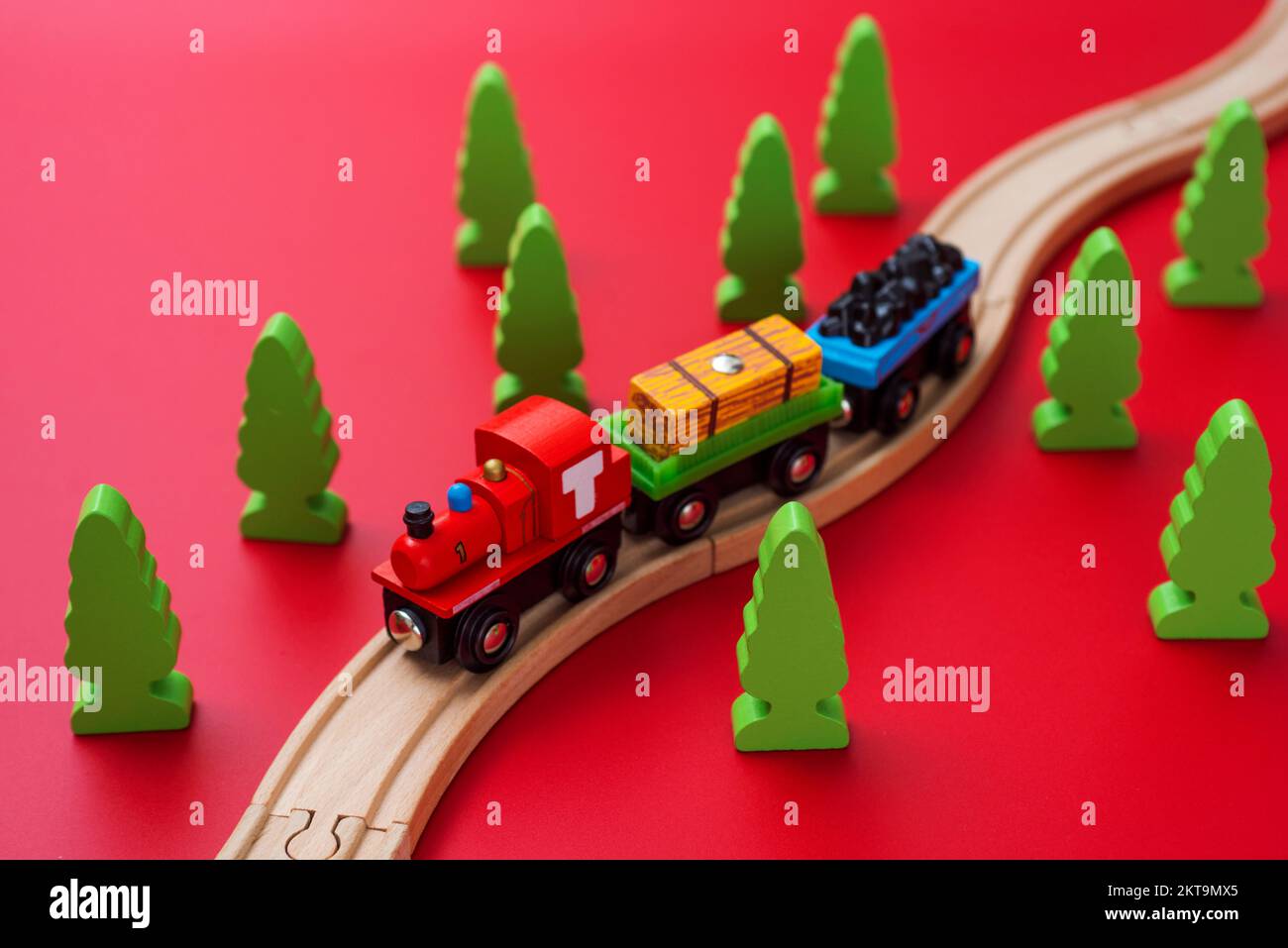 Wooden toy train on the railroad among green trees on red background ...