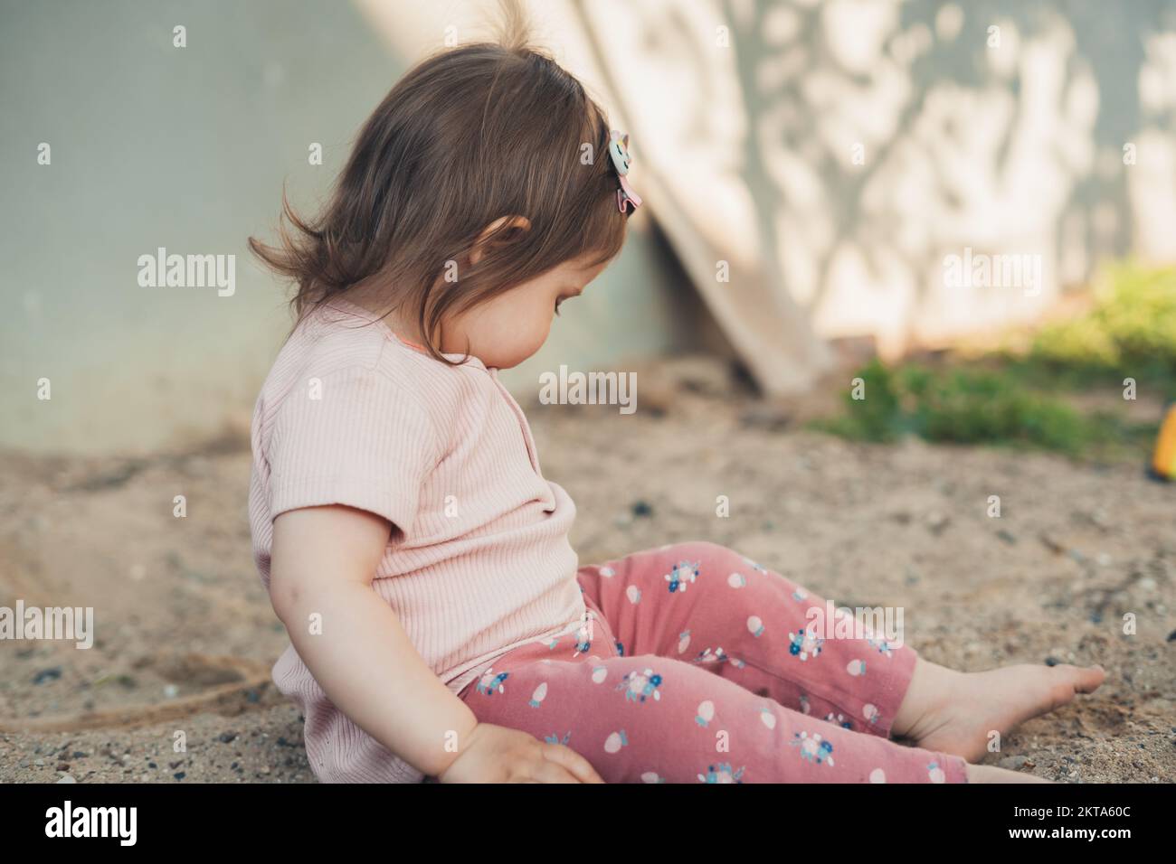 Little girl exploring a pile of sand, touching it, gathering the sand ...