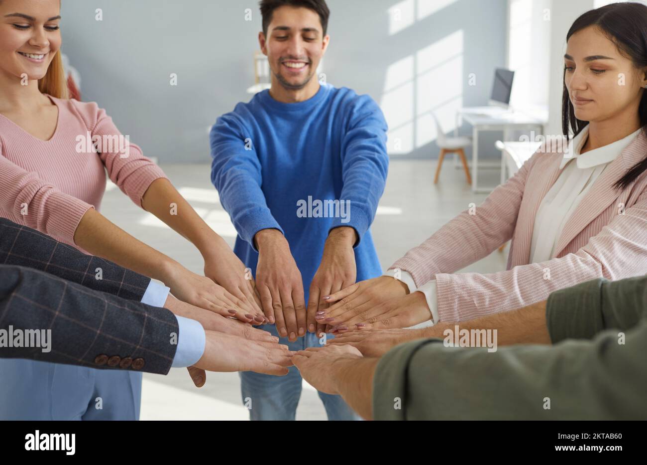 Team of happy young business men and women putting their hands together ...