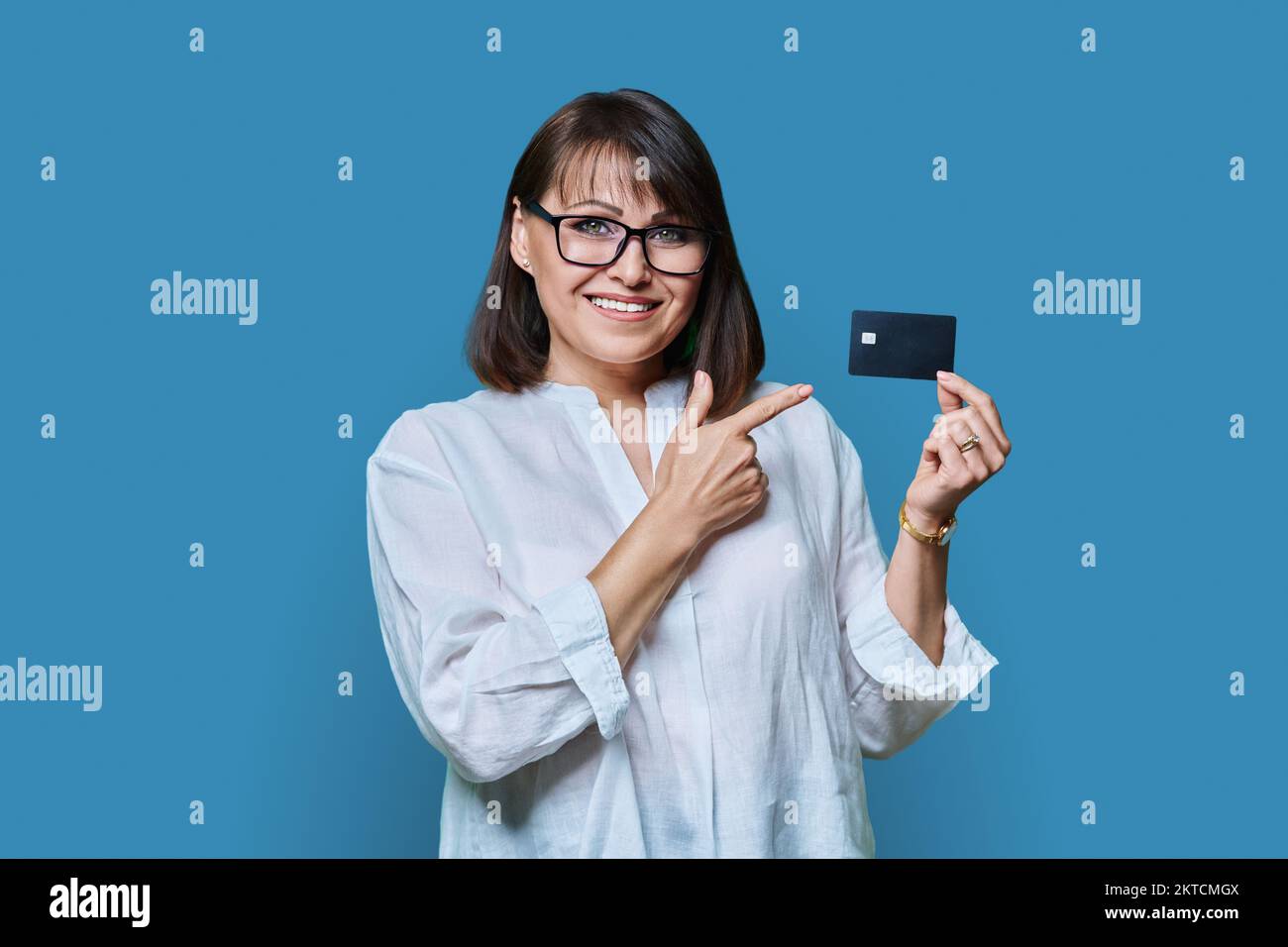 Attractive middle aged smiling woman holding plastic credit card, blue ...