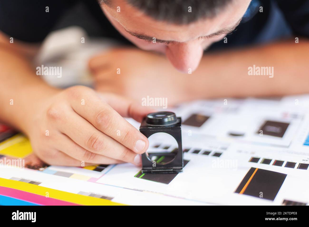 Young man in the process of printing used color scales and loupe and ...