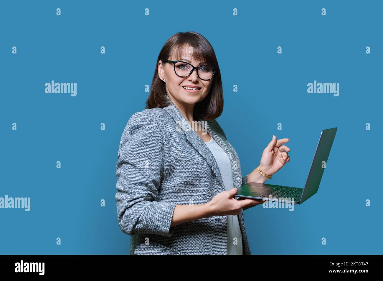 Middle age business woman with laptop looking at camera on blue ...
