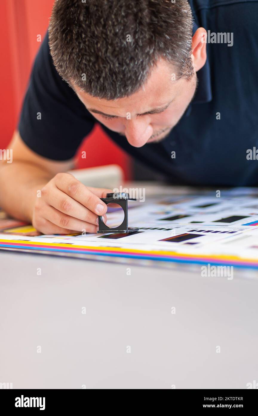 Young man in the process of printing used color scales and loupe and ...