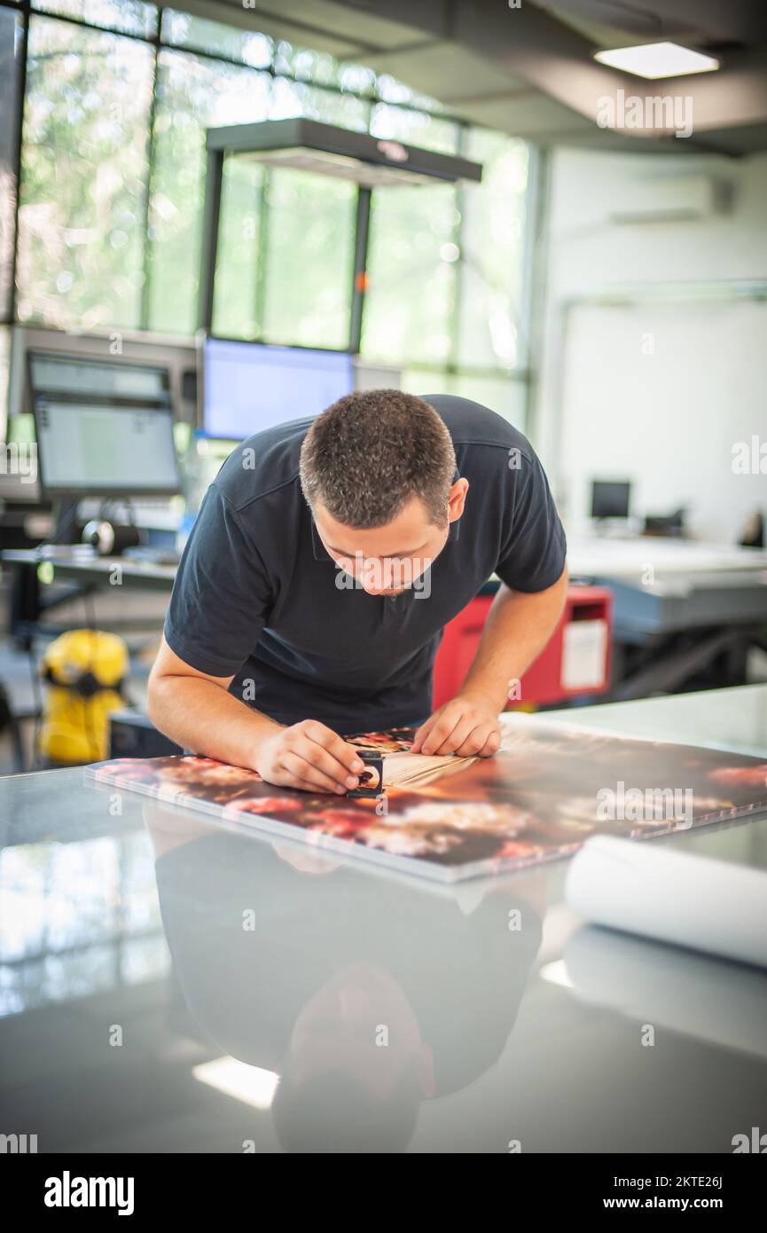 Young man in the process of printing used color scales and loupe and ...