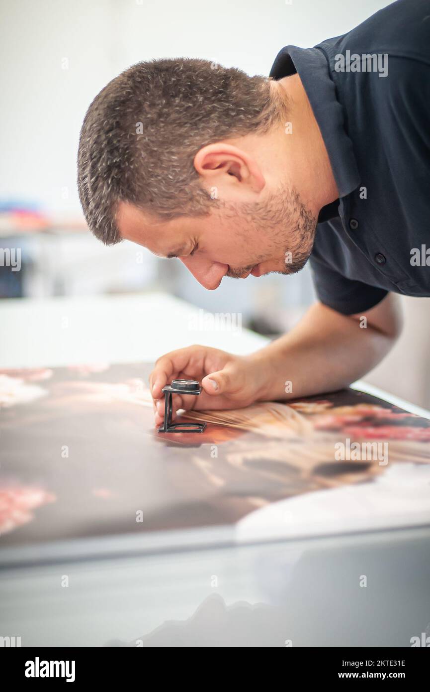 Young man in the process of printing used color scales and loupe and ...
