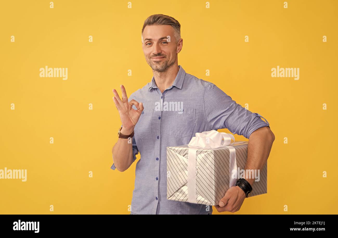 happy guy with gift box show ok gesture on yellow background, shopping ...