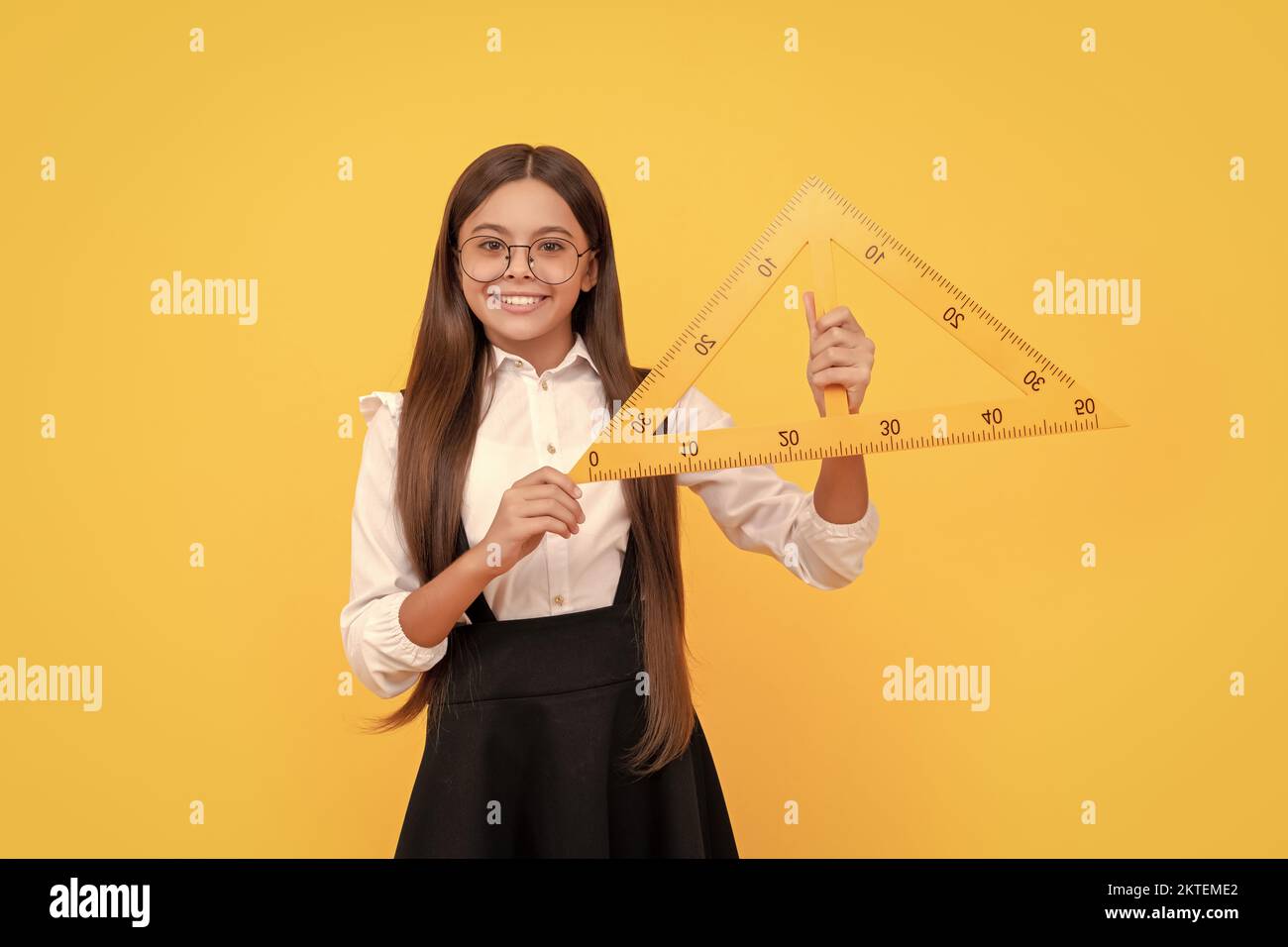 cheerful child in school uniform and glasses hold mathematics triangle ...