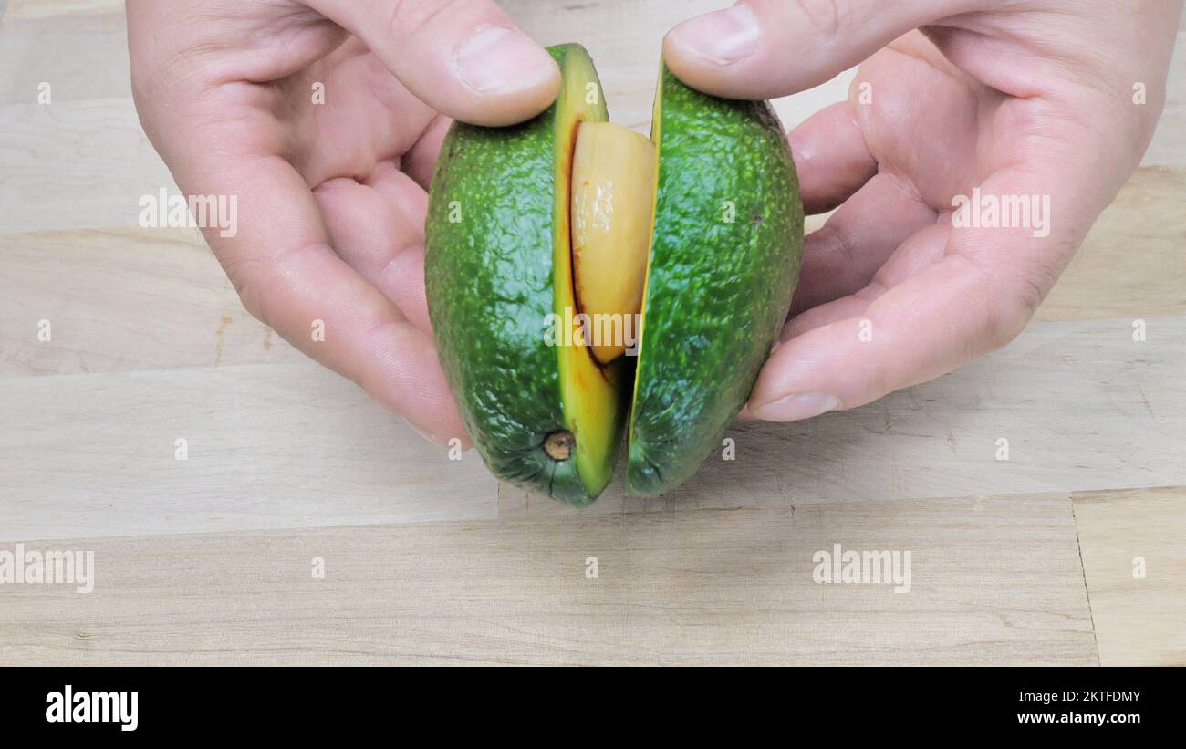 Closeup on hands holding fresh avocado cut in half on light background ...
