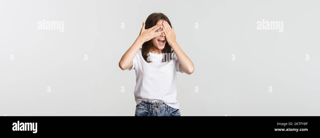Excited and curious girl shut eyes and peeking through fingers amused ...