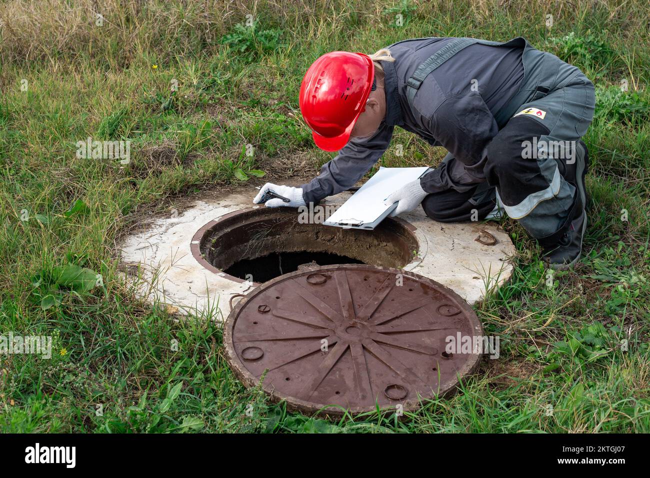 A man working plumber in overalls bent over a water well fixes the ...