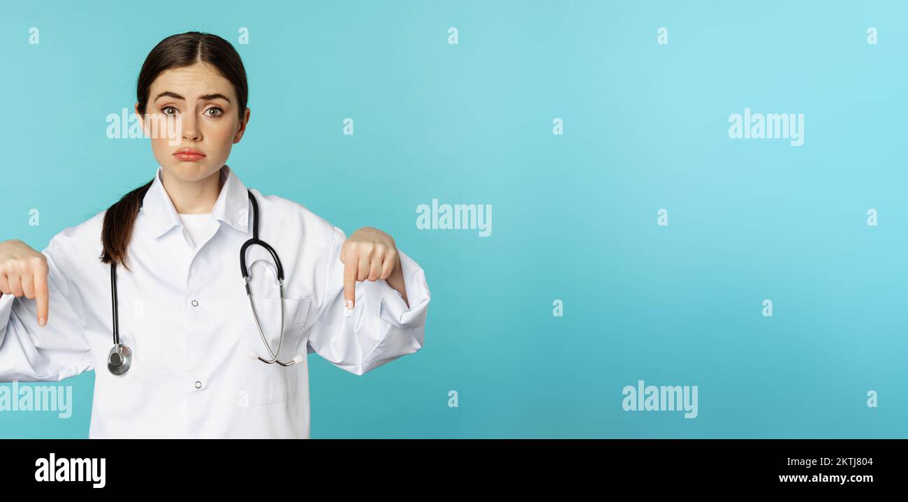 Sad and gloomy doctor, female medical worker pointing fingers down ...