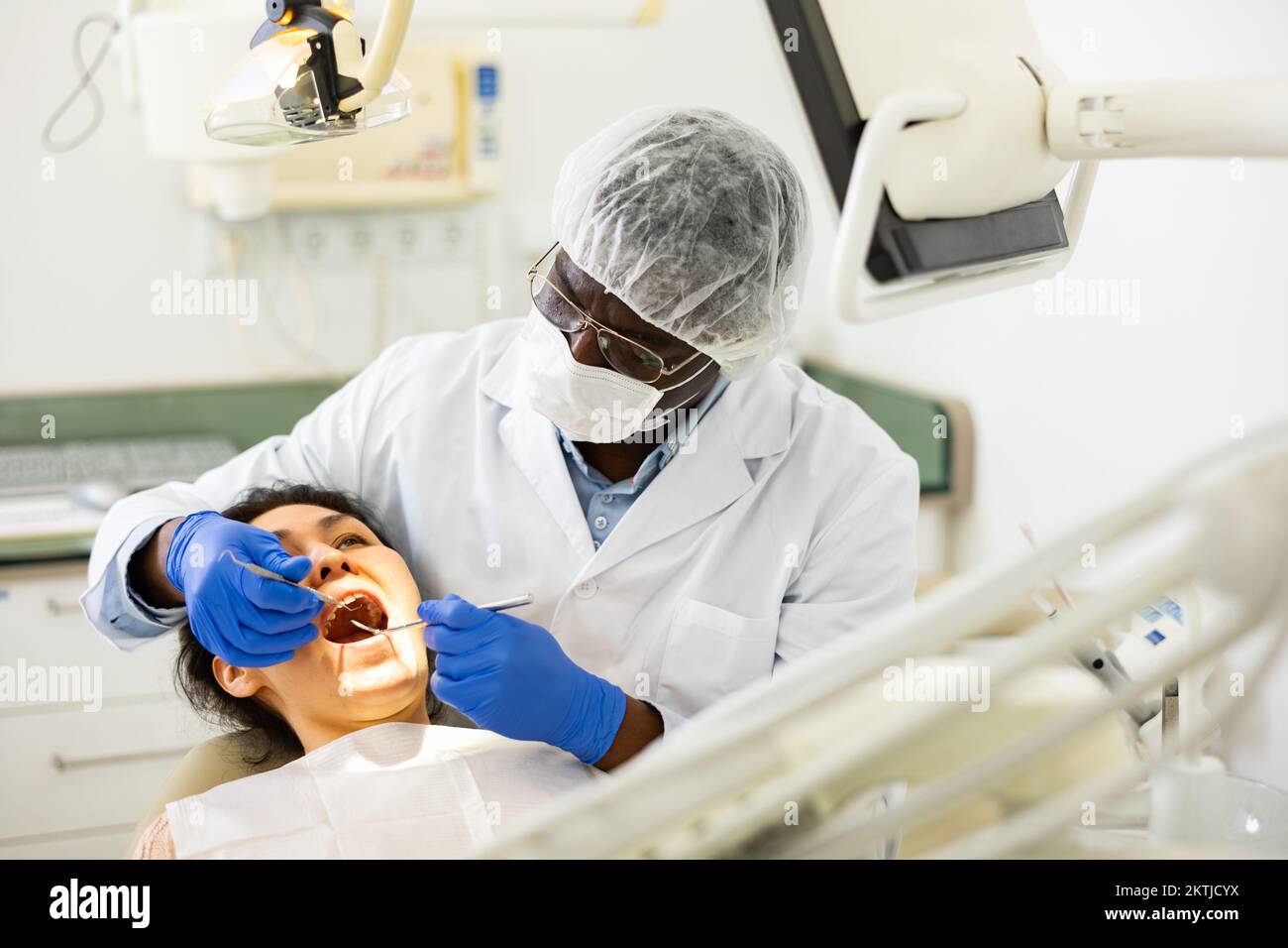 Dentist in face mask inspects female patient teeth with mirror Stock ...