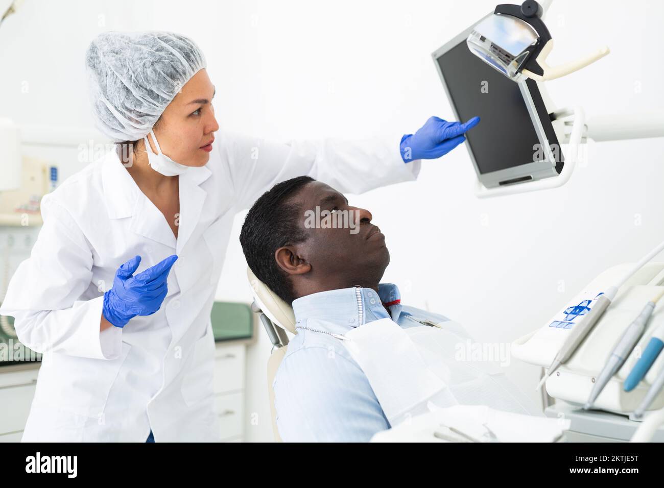 Female dentist explaining X-ray on computer display to patient at ...