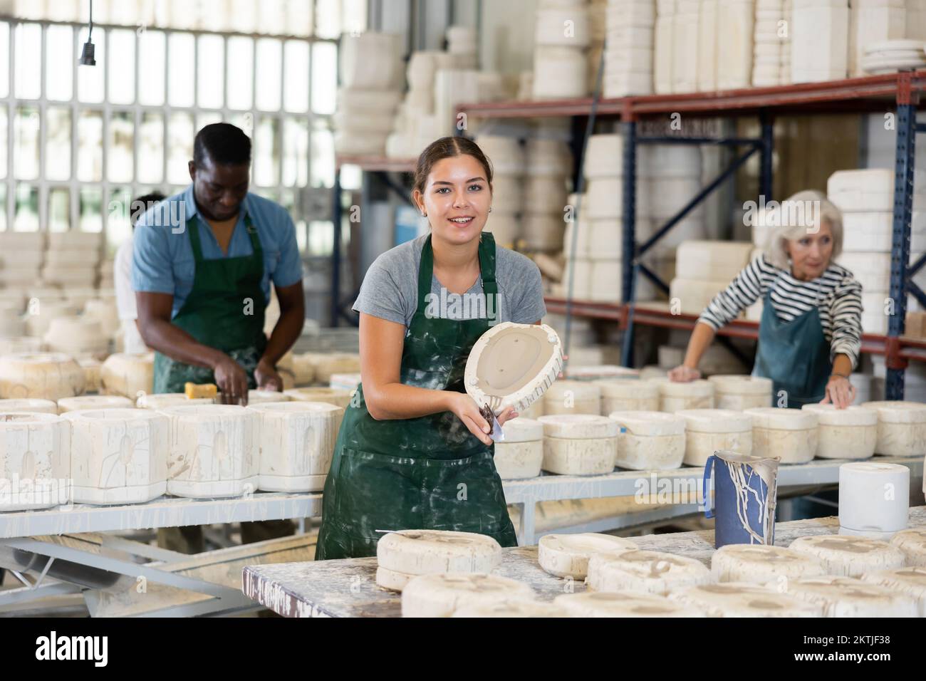 Positive young worker demonstrates half of plaster mold for pottery in ...