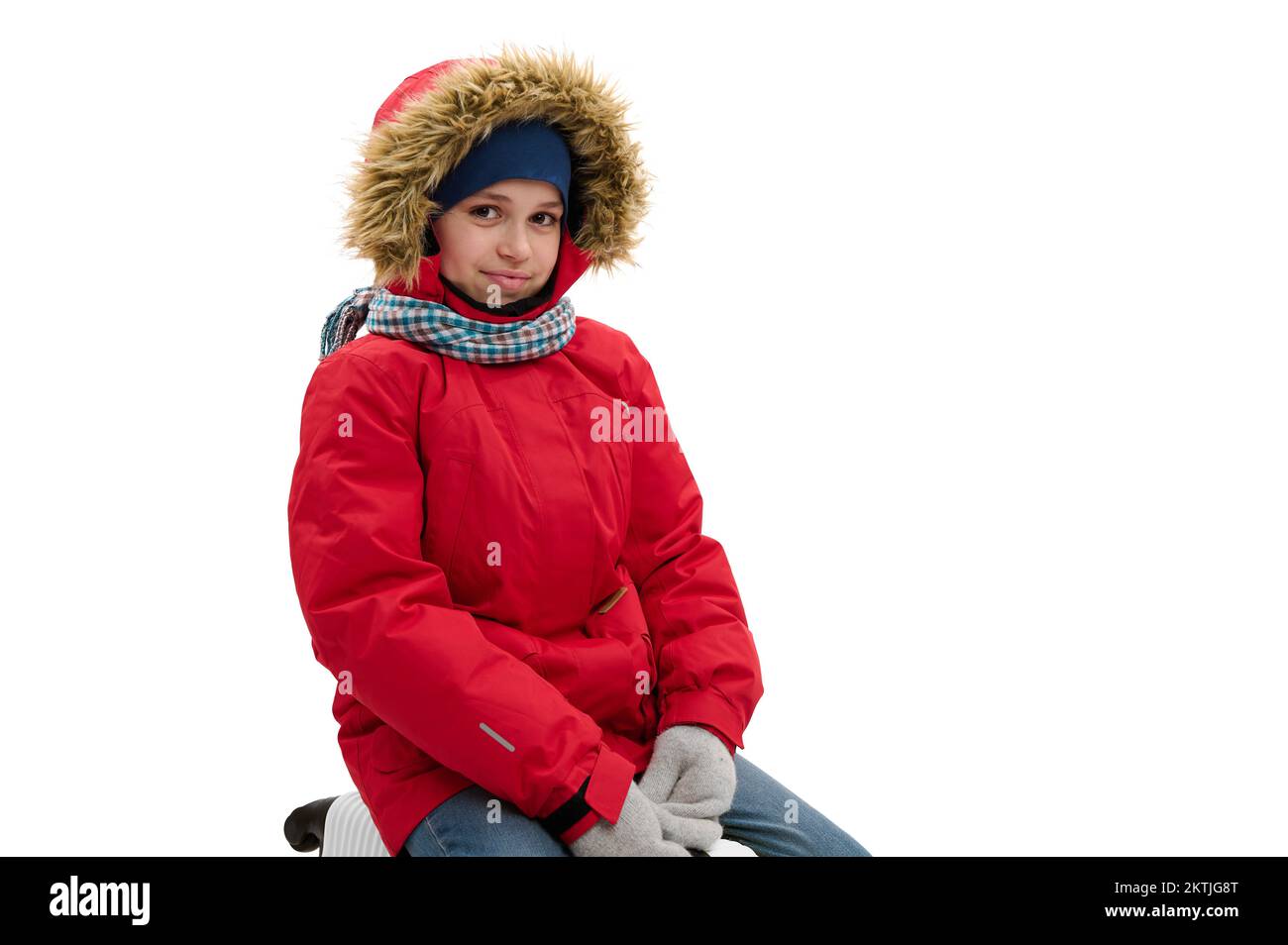 Lovely teenager traveler boy in red parka with fur hood, blue jeans and wool mittens, cutely ...