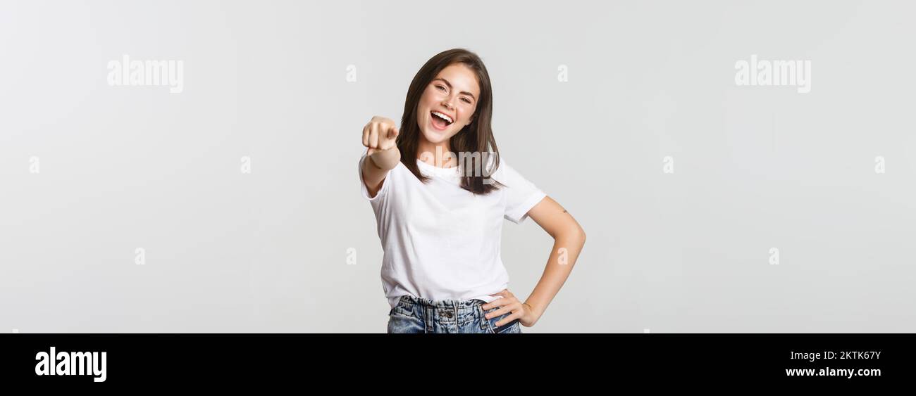 Smiling cheerful brunette girl pointing finger at camera, congratulate ...