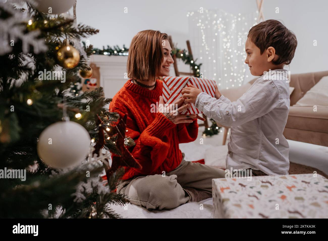 Lovely boy giving present to his mother under the Christmas tree Stock ...