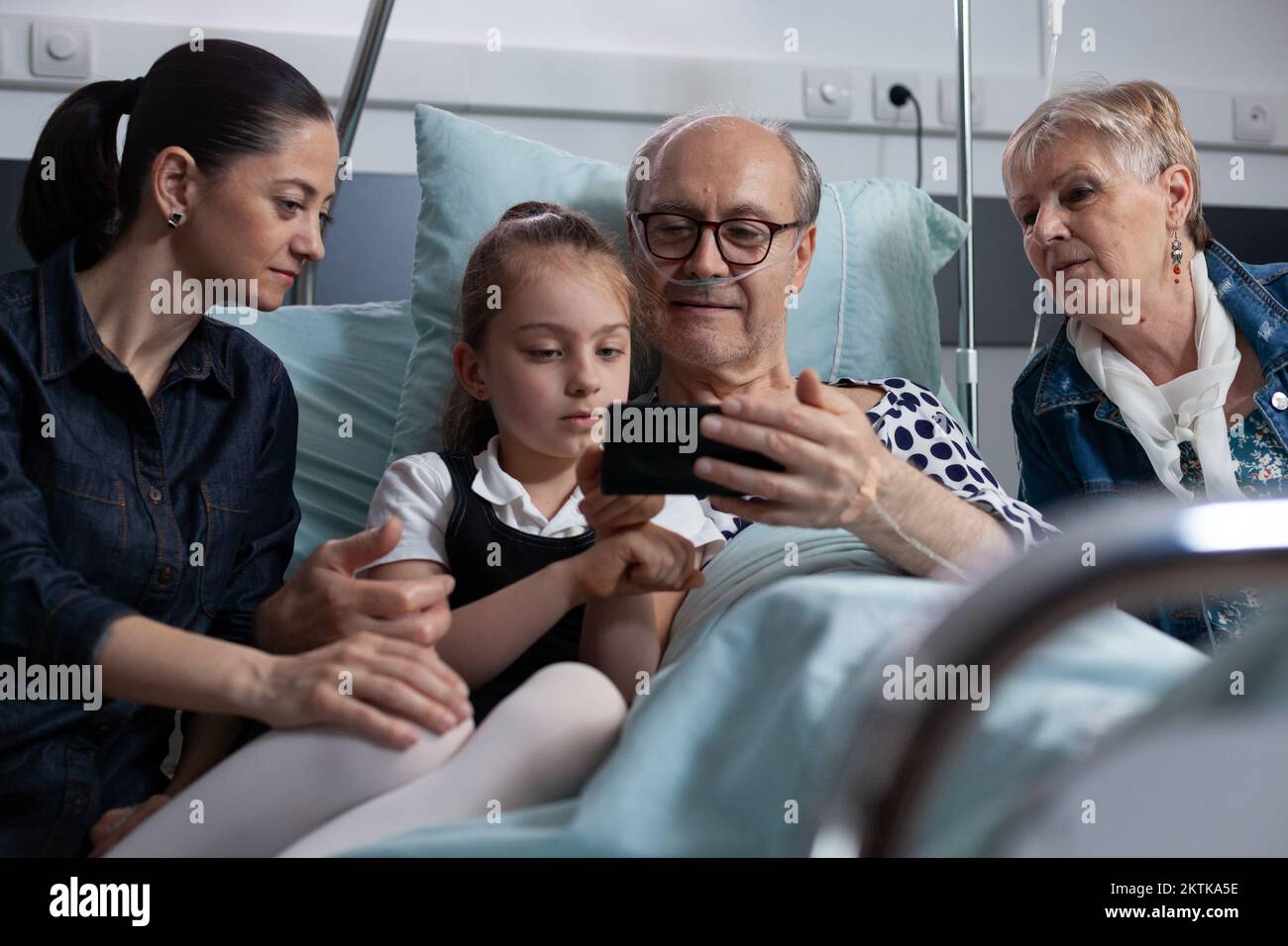 Young woman, daughter showing how cell phone works to sick grandfather ...