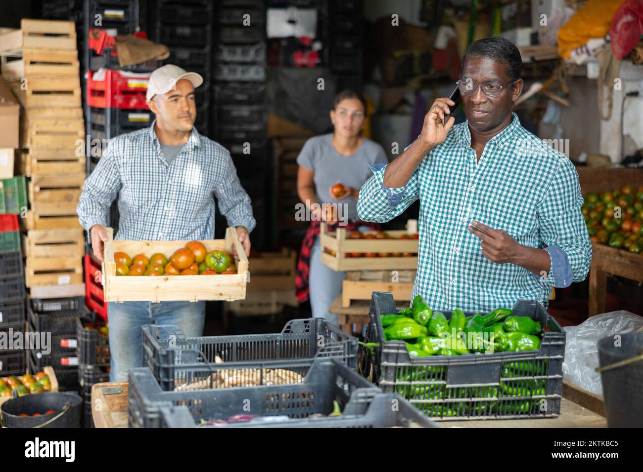 Owner of vegetable warehouse is talking on mobile phone while other ...
