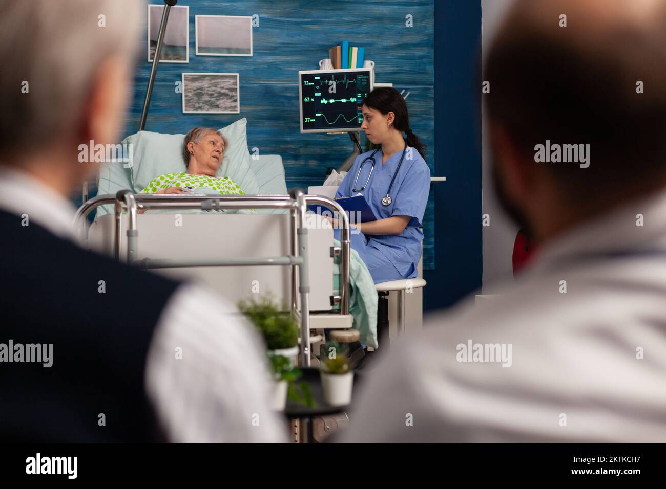 Elderly woman lying in hospital clinic bed talking to nurse about ...