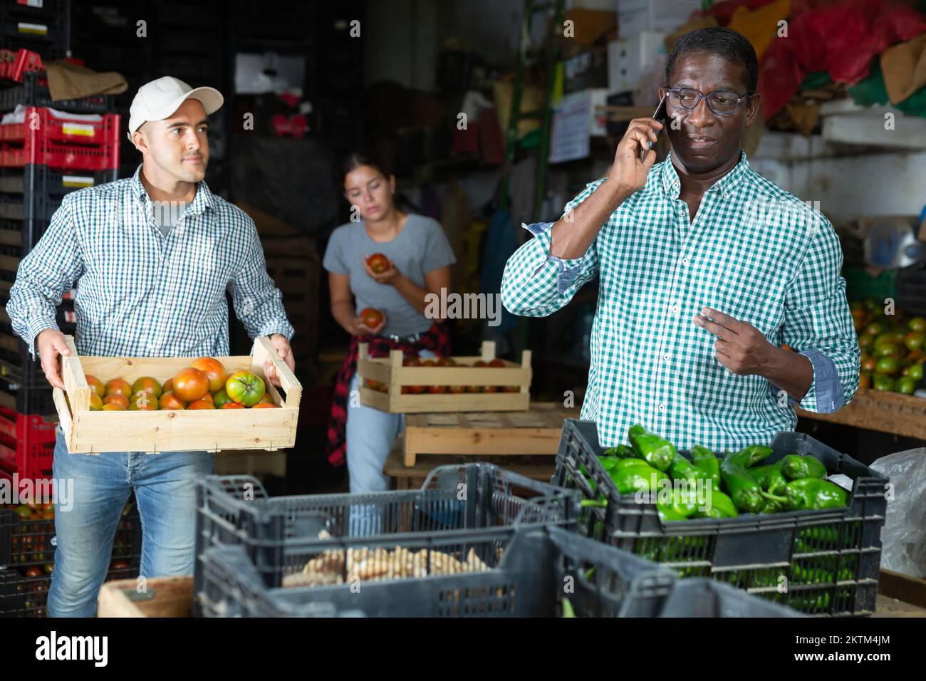 Owner of vegetable warehouse is talking on mobile phone while other ...