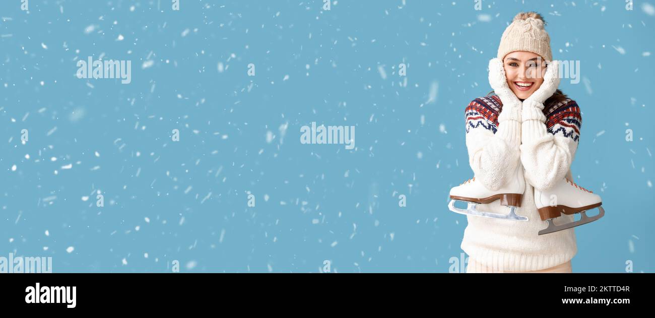 Happy young woman in winter clothes and with ice skates on light blue ...