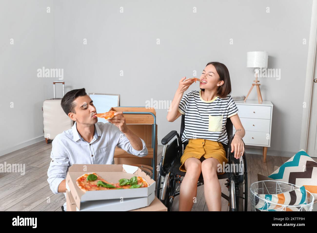 Young man and his wife in wheelchair eating pizza in their new flat on ...