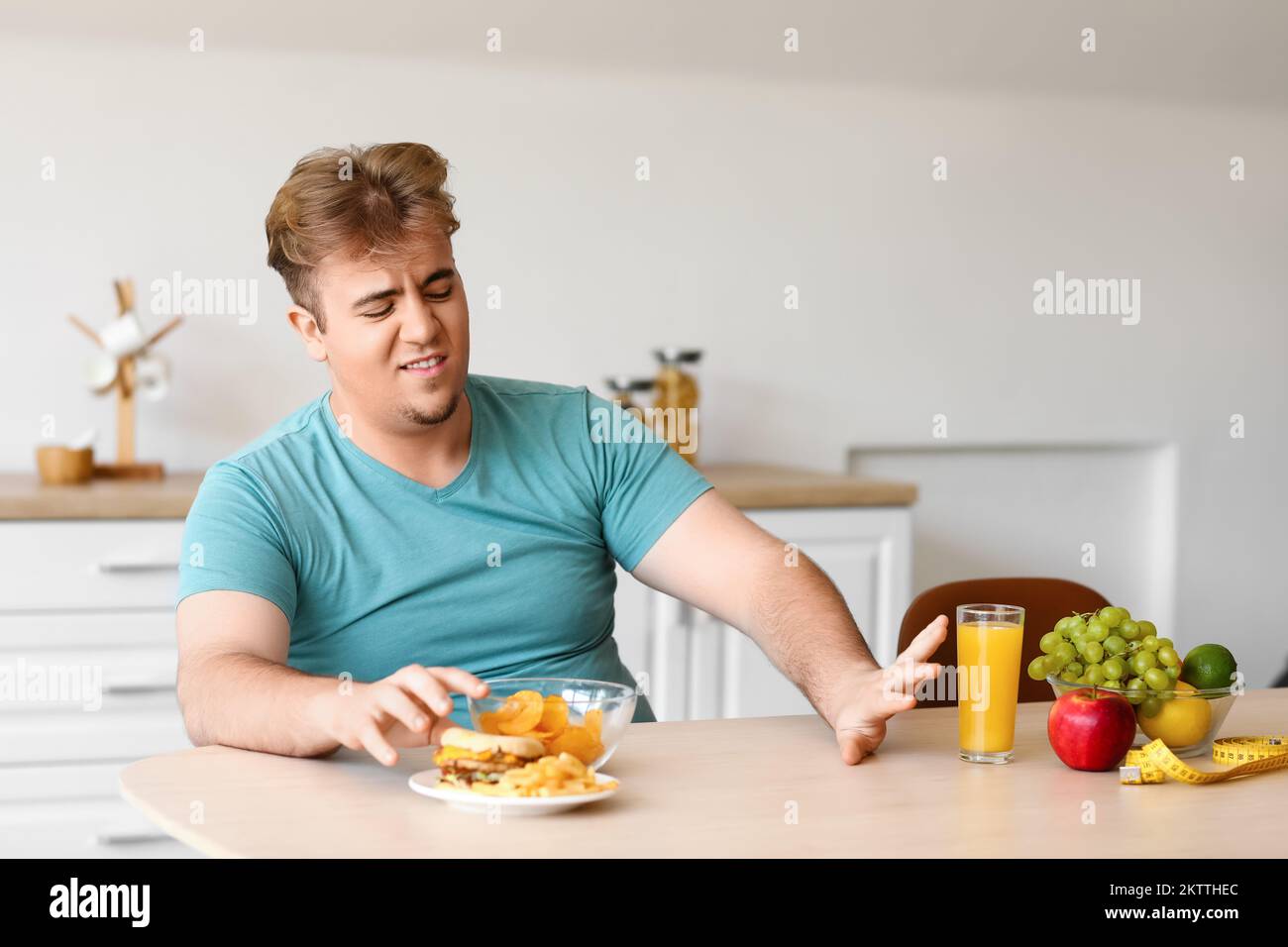 Young overweight man rejecting healthy food at table in kitchen Stock ...