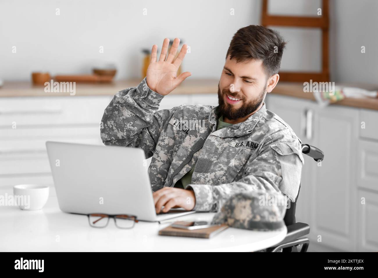 Young soldier in wheelchair video chatting at table in kitchen Stock ...