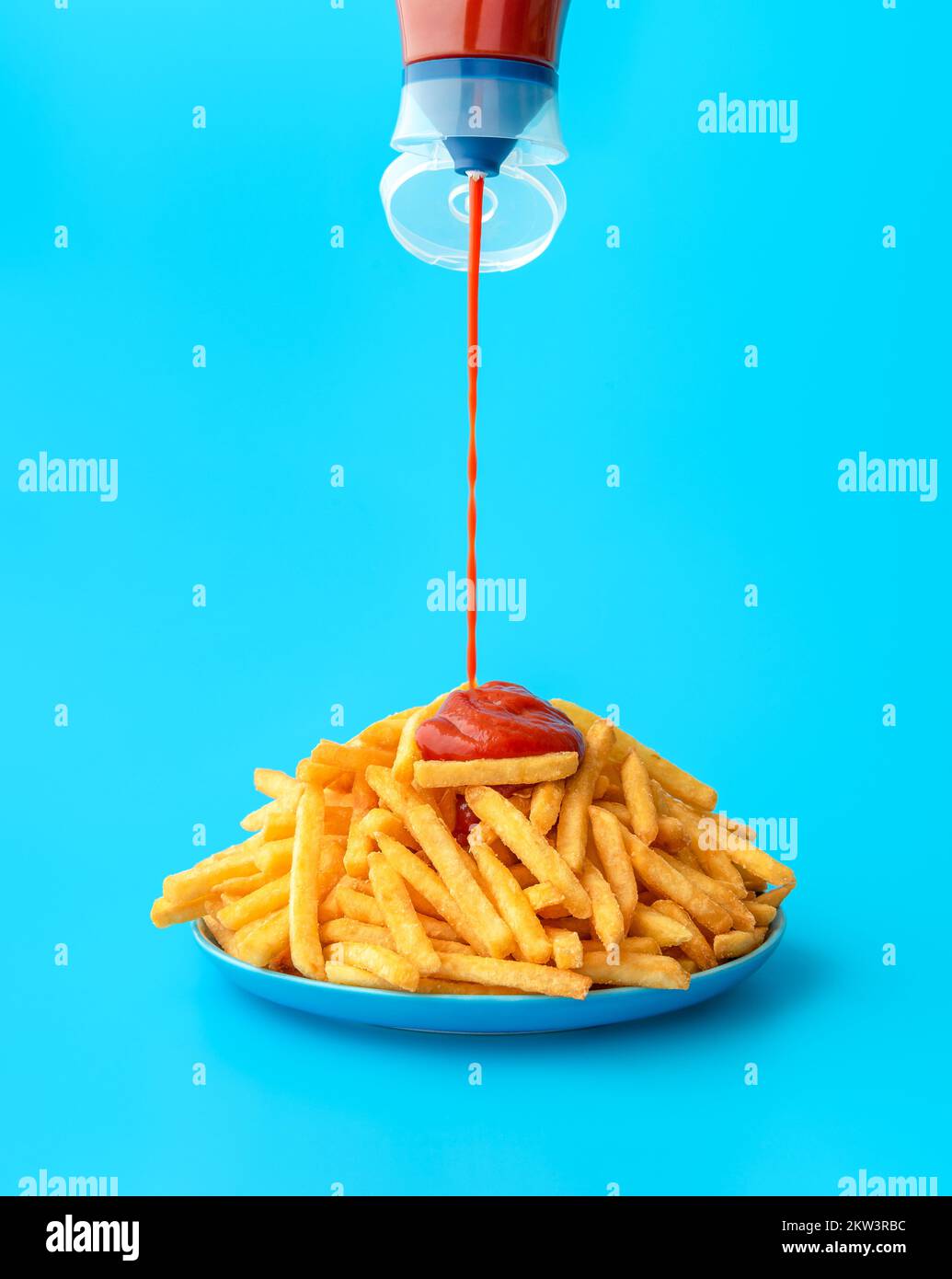 Pouring ketchup from a bottle over french fries, minimalist on a blue ...