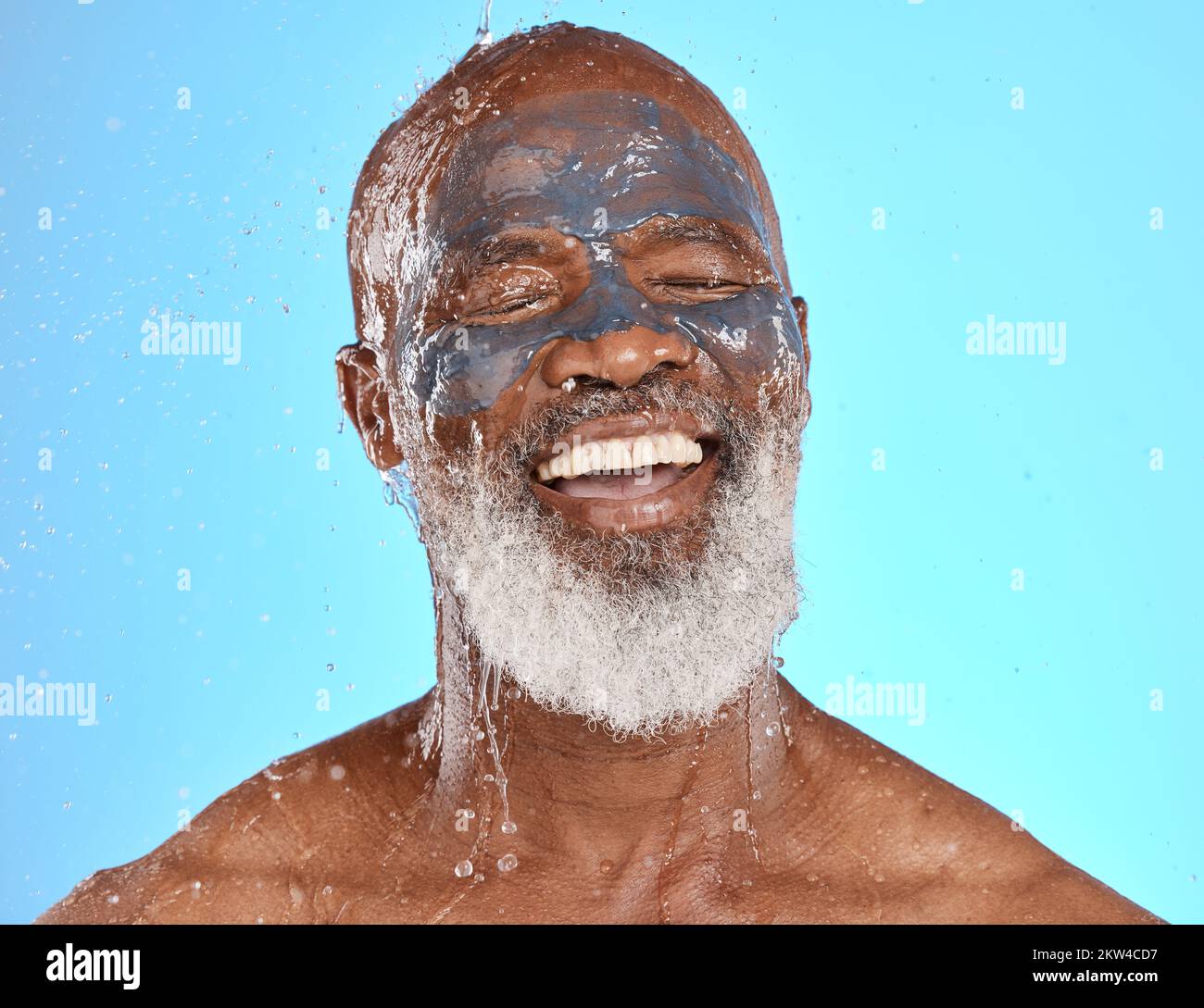 Face, water splash and senior black man in clay mask in studio isolated on a blue background ...