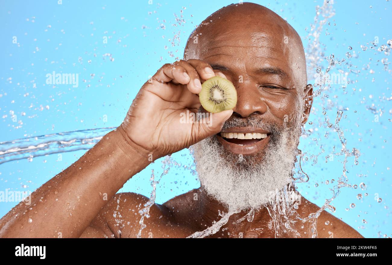 Skincare, kiwi and senior man in studio for beauty, water splash and wellness on blue background ...