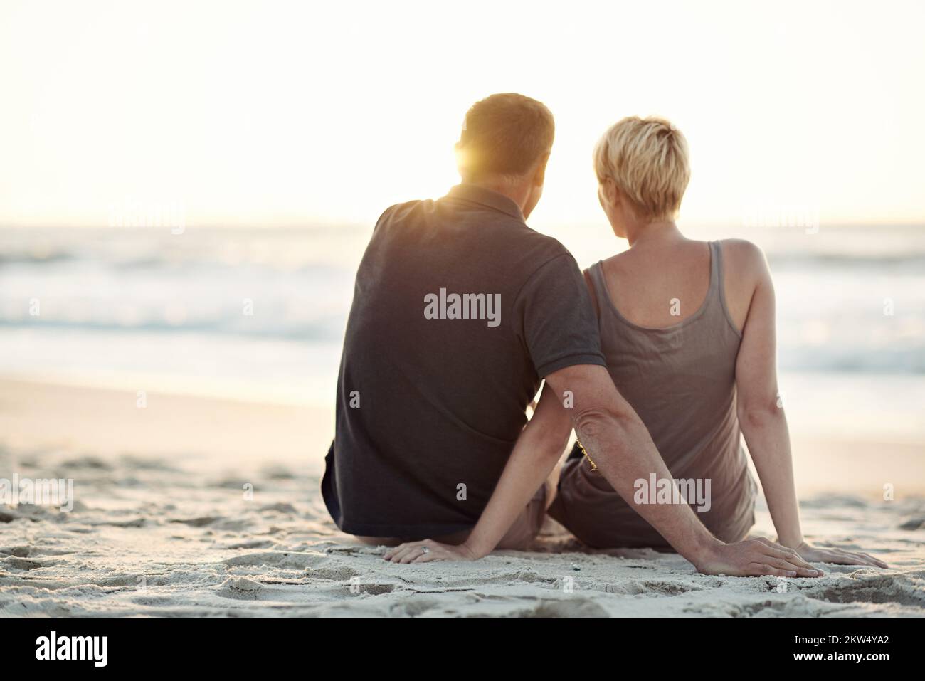 Taking in a quiet sunset. A loving couple sitting on the beach - rear ...