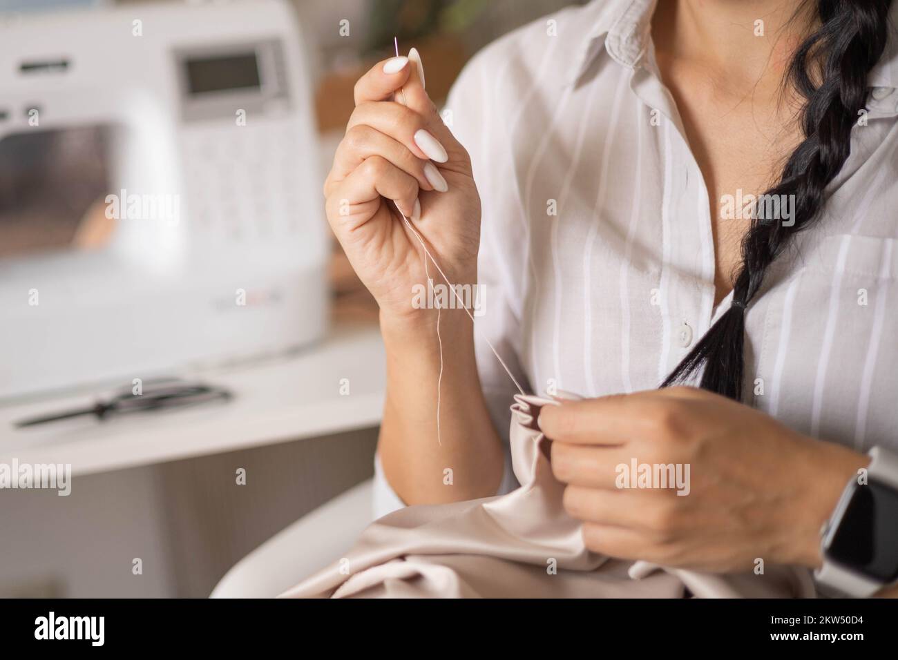 Female tailor hands sewing beige textile with needle and thread process ...