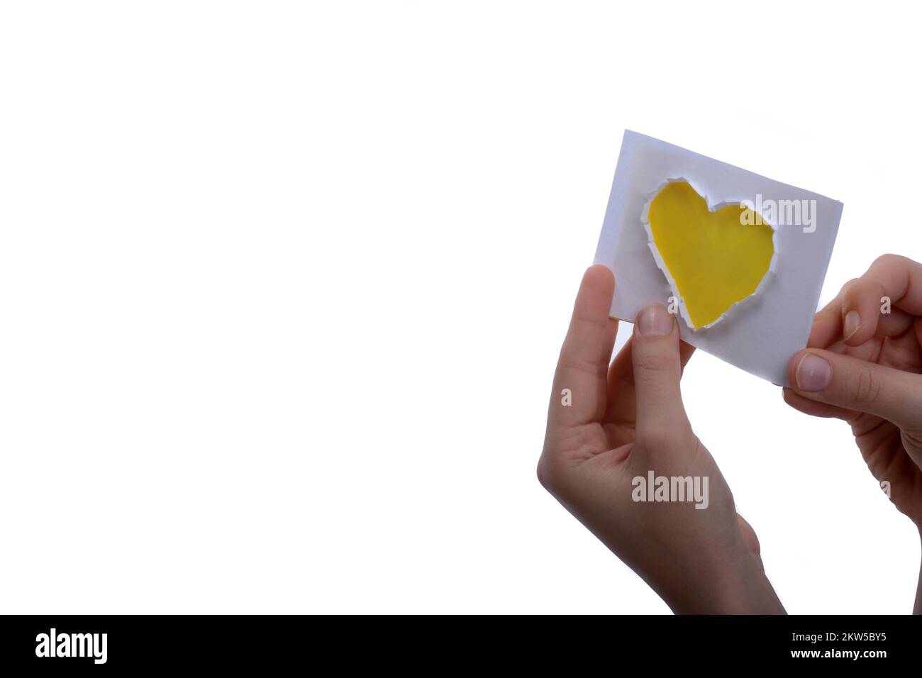 Hand holding a yellow heart shape paper cut out of paper on a white ...