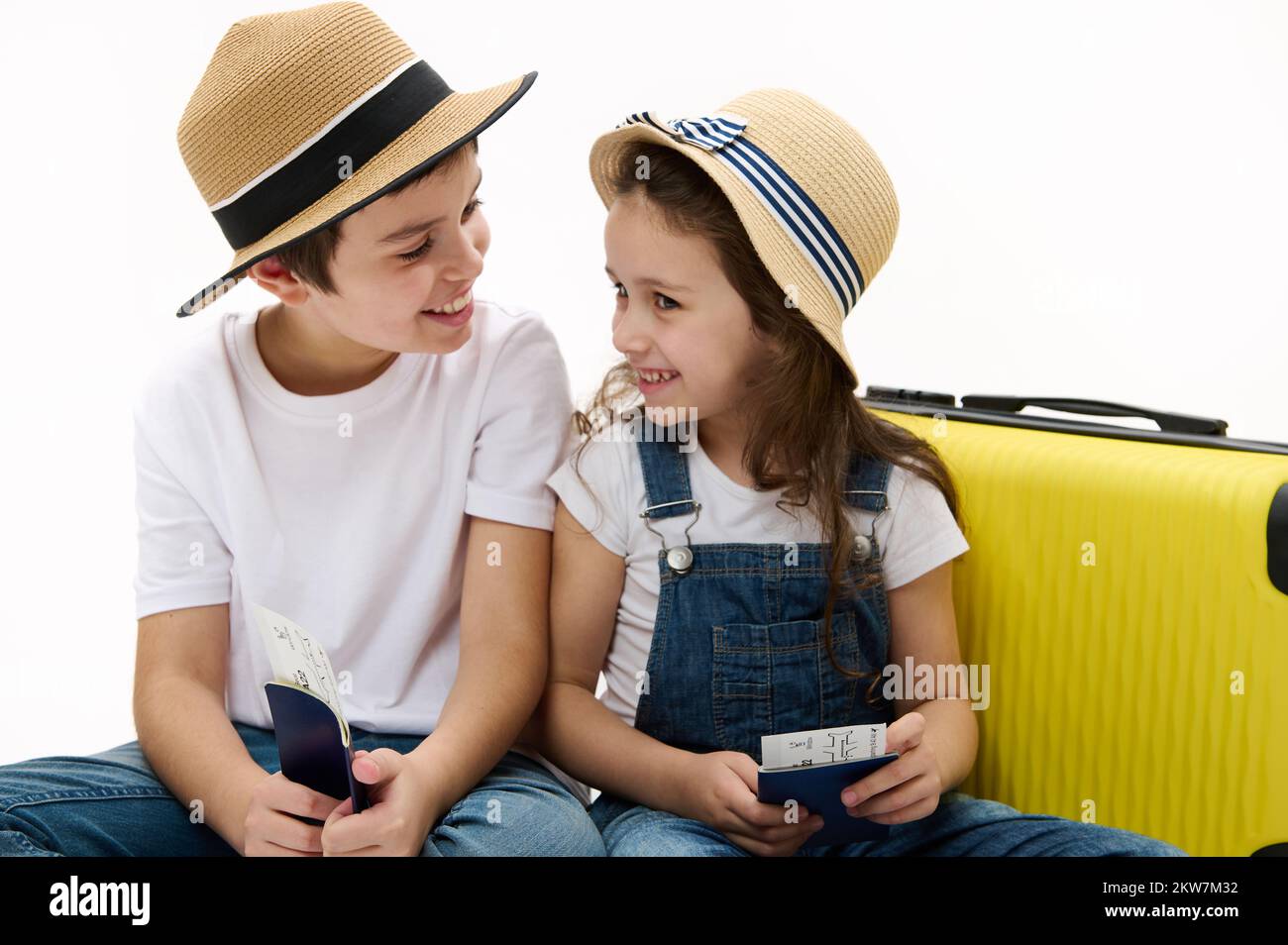 Happy kids travelers with boarding pass, sit against yellow suitcase ...