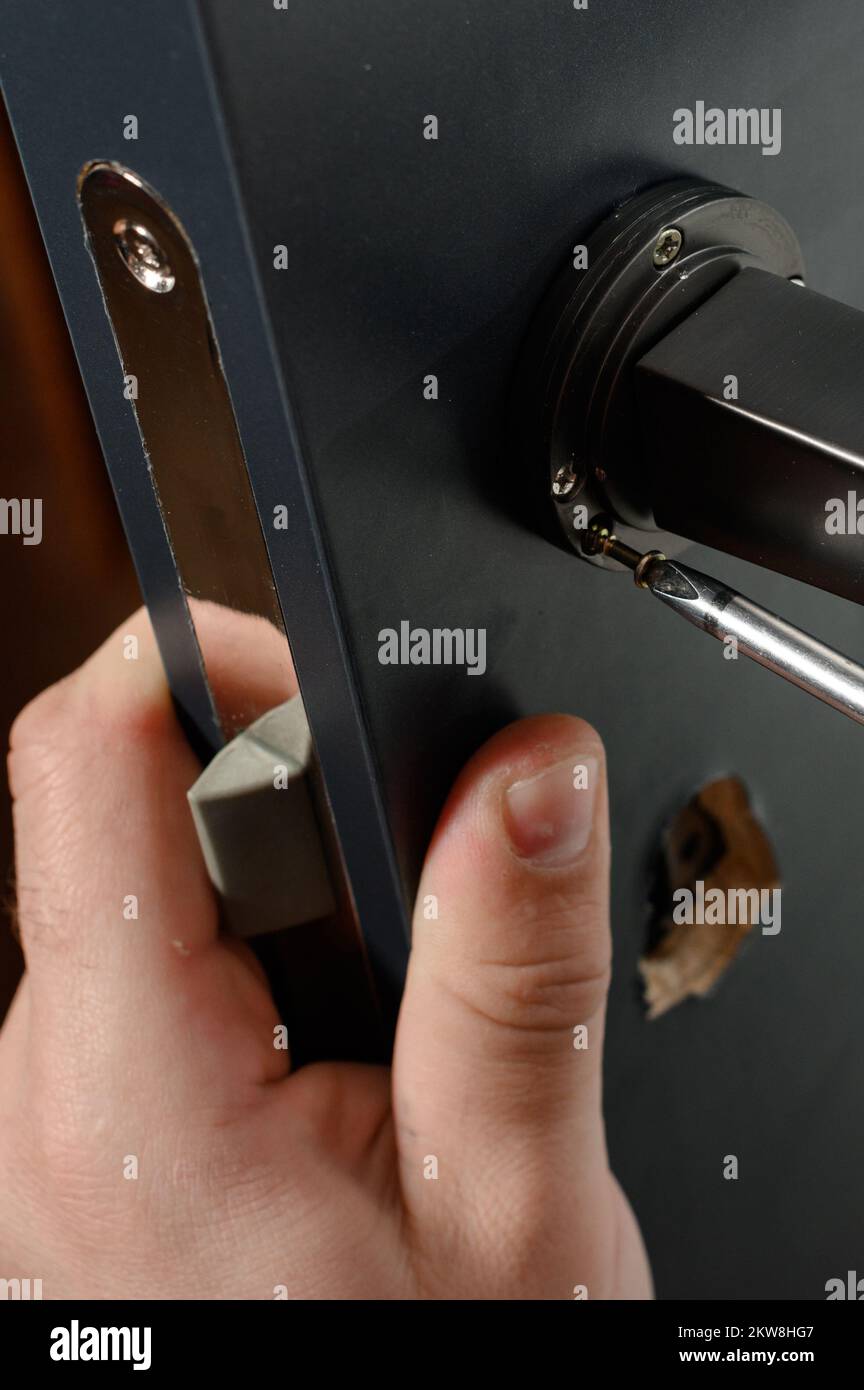 A man installs a door handle in a door, carpentry work at home, repair ...