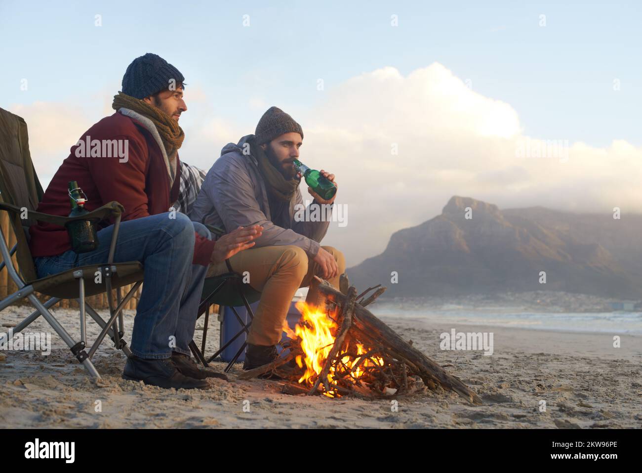 Beach beers and a fire. Two young men sitting around a fire on the ...