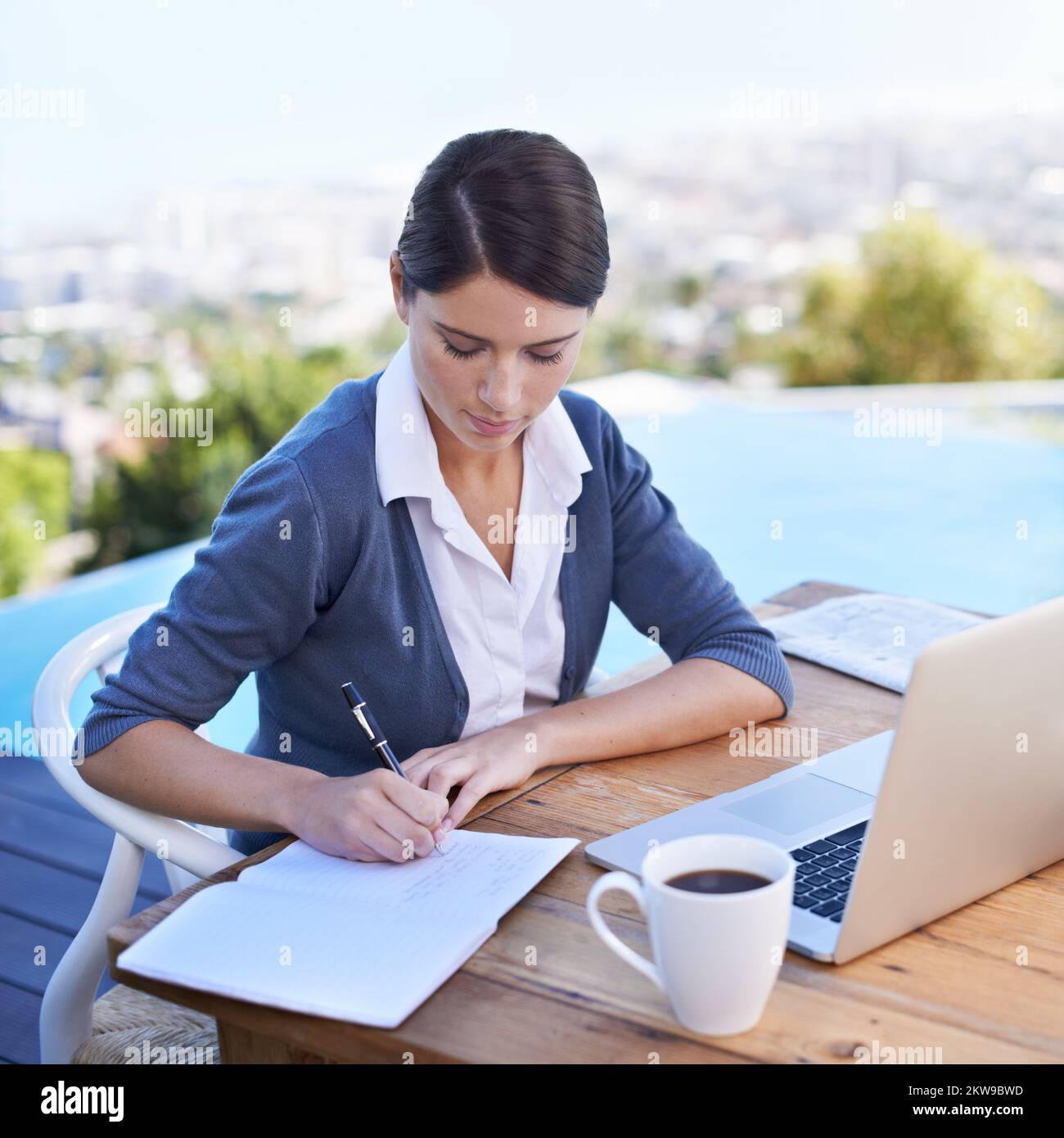 Taking notes. a young businesswoman working on her laptop by a swimming ...