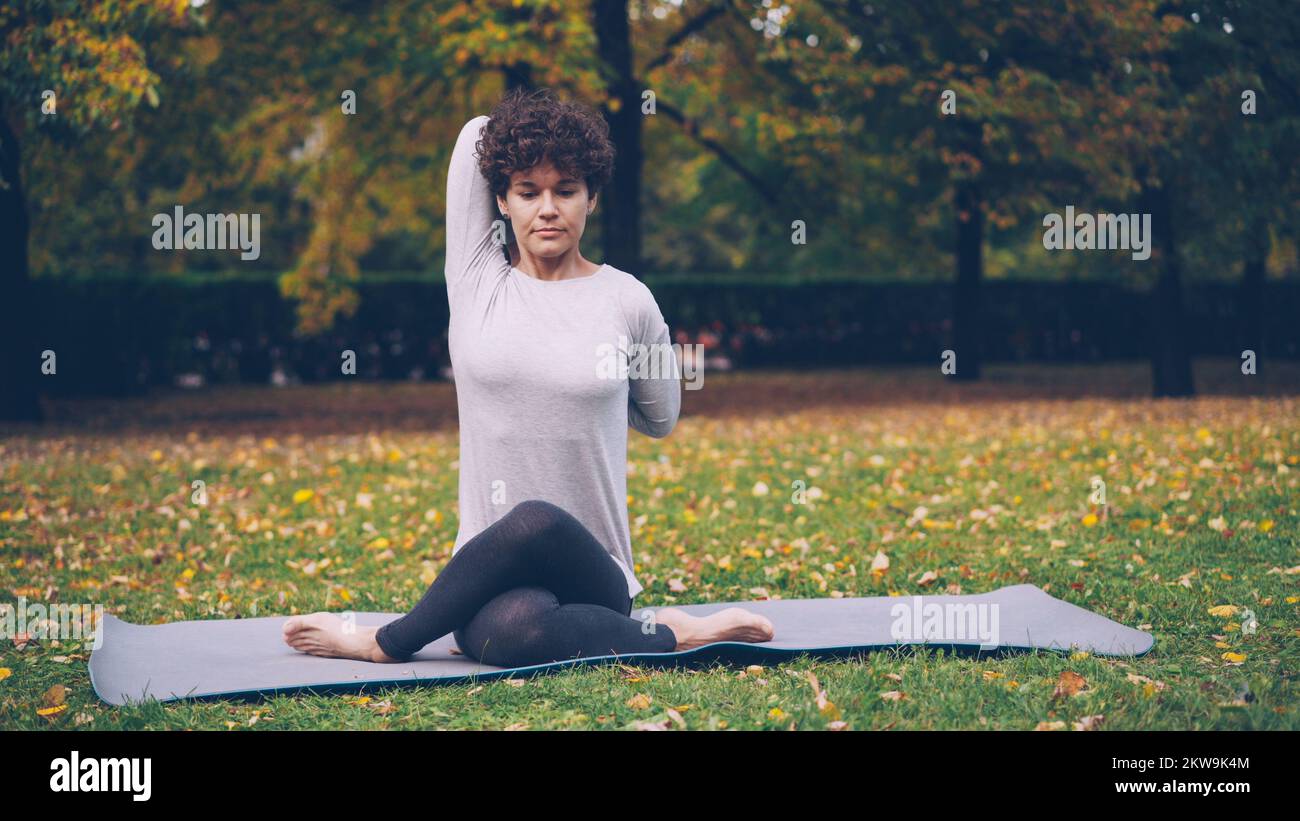 Serious young woman yogini is training in park sitting in Cow Face pose ...