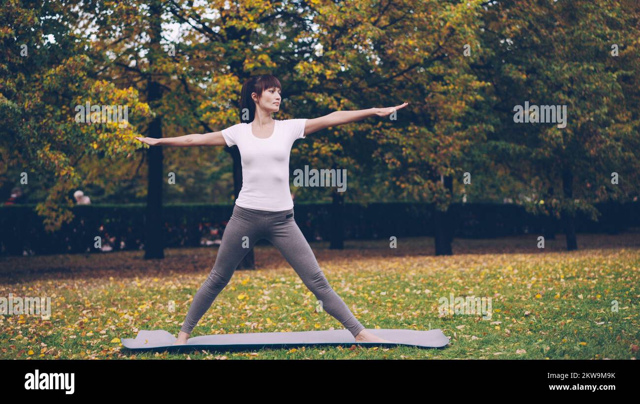Attractive young woman is doing yoga outdoors standing on mat and ...