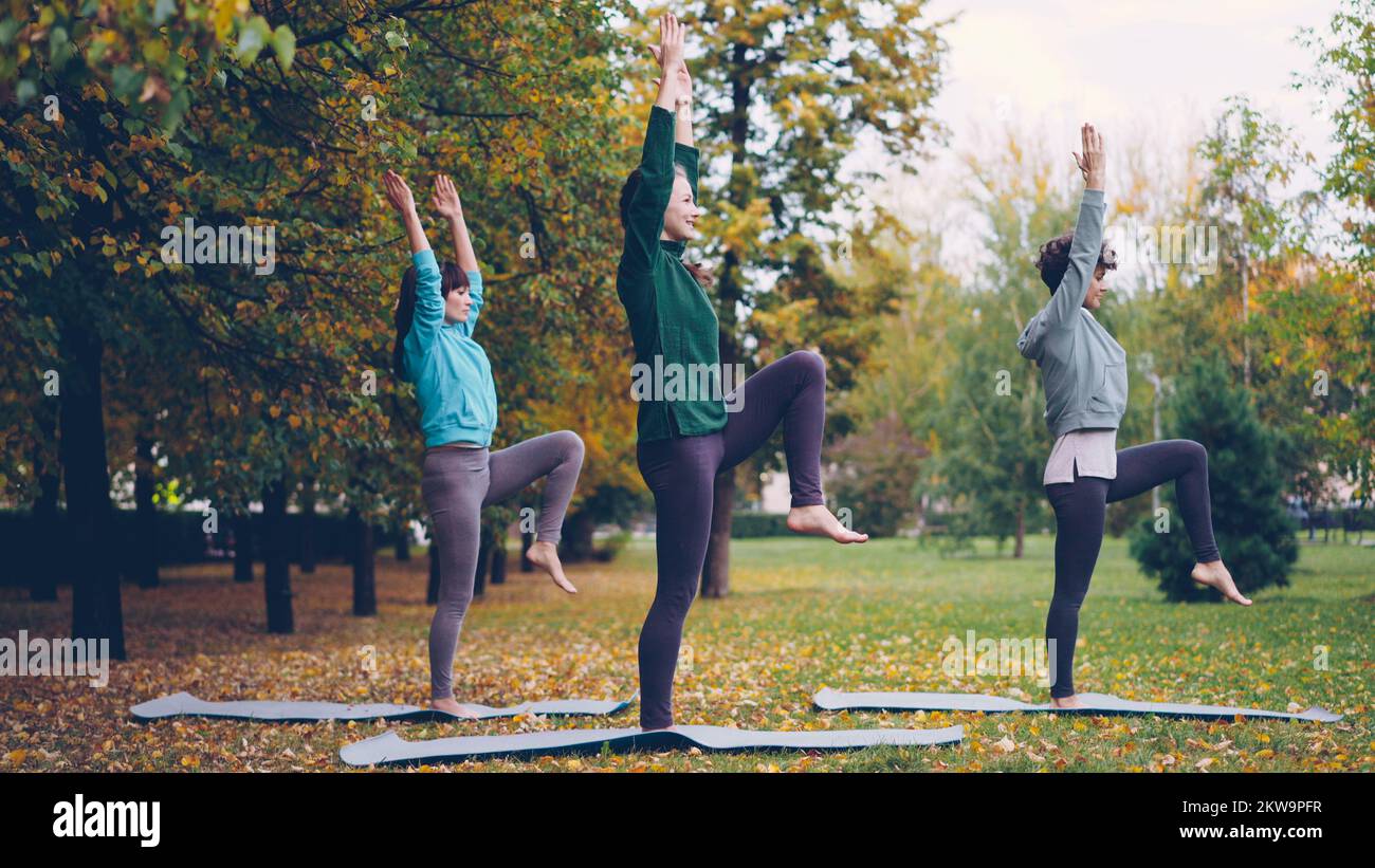 Slender young women are exercising outdoors in park bending forwards ...