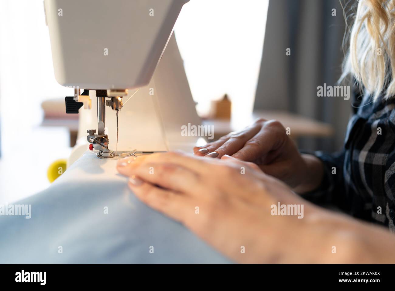 Close up view of sewing process. Female hands stitching blue fabric on ...