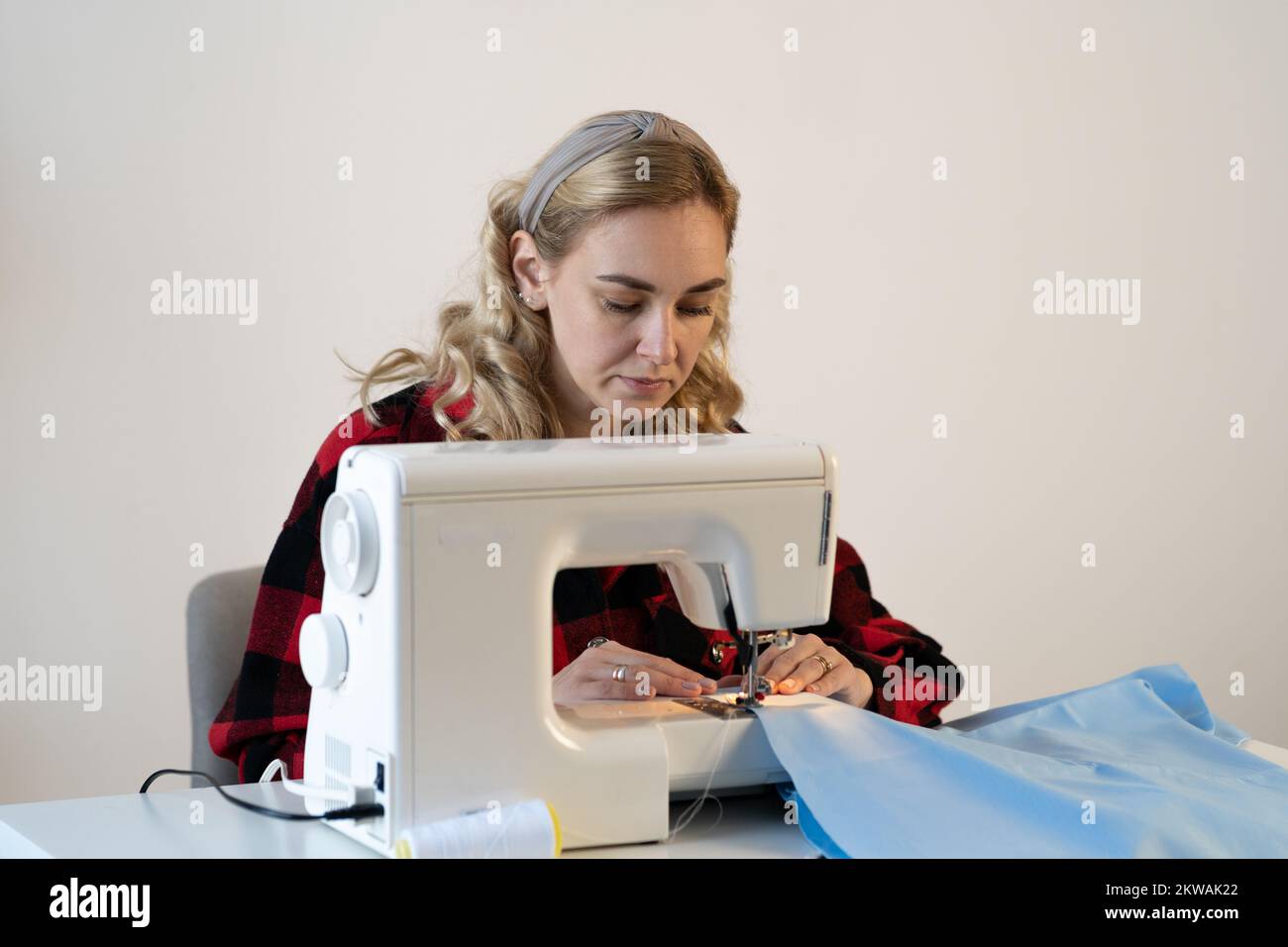 Cheerful young woman sewing while sitting at her working place in ...