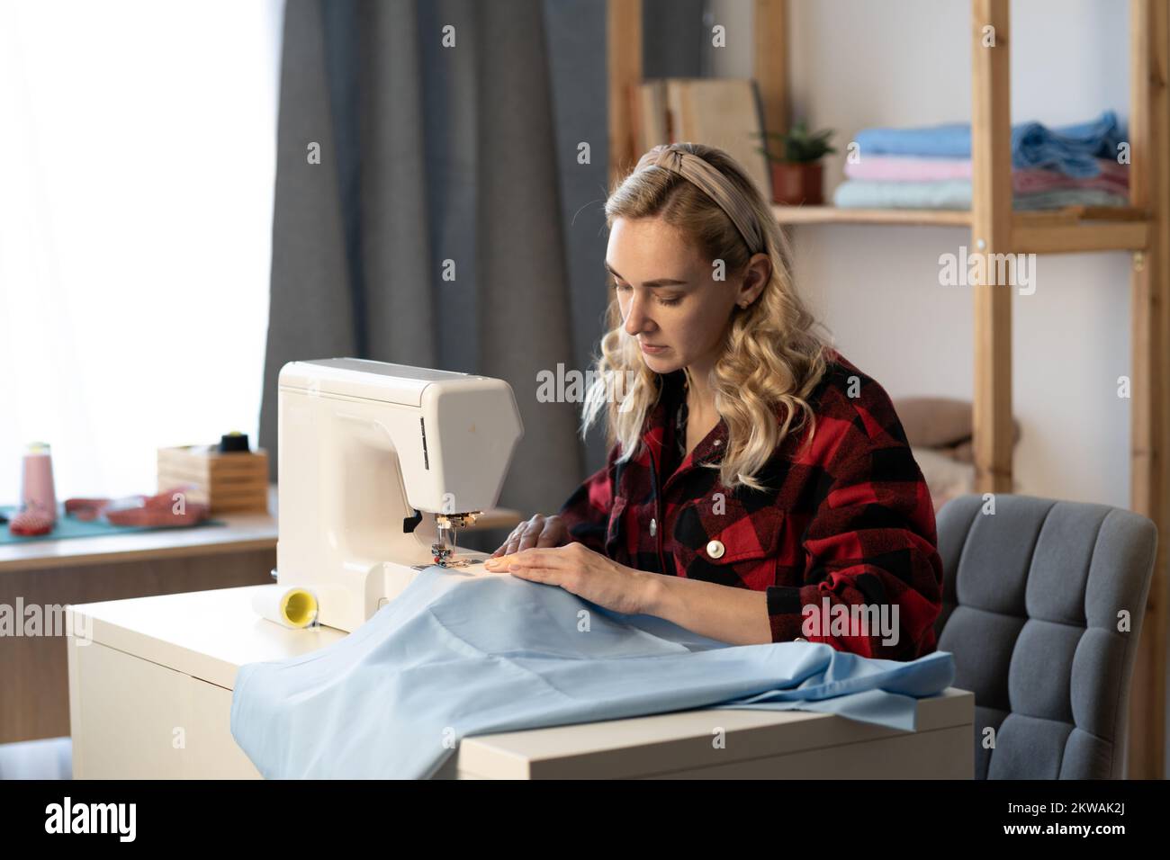 Cheerful young woman sewing while sitting at her working place in ...