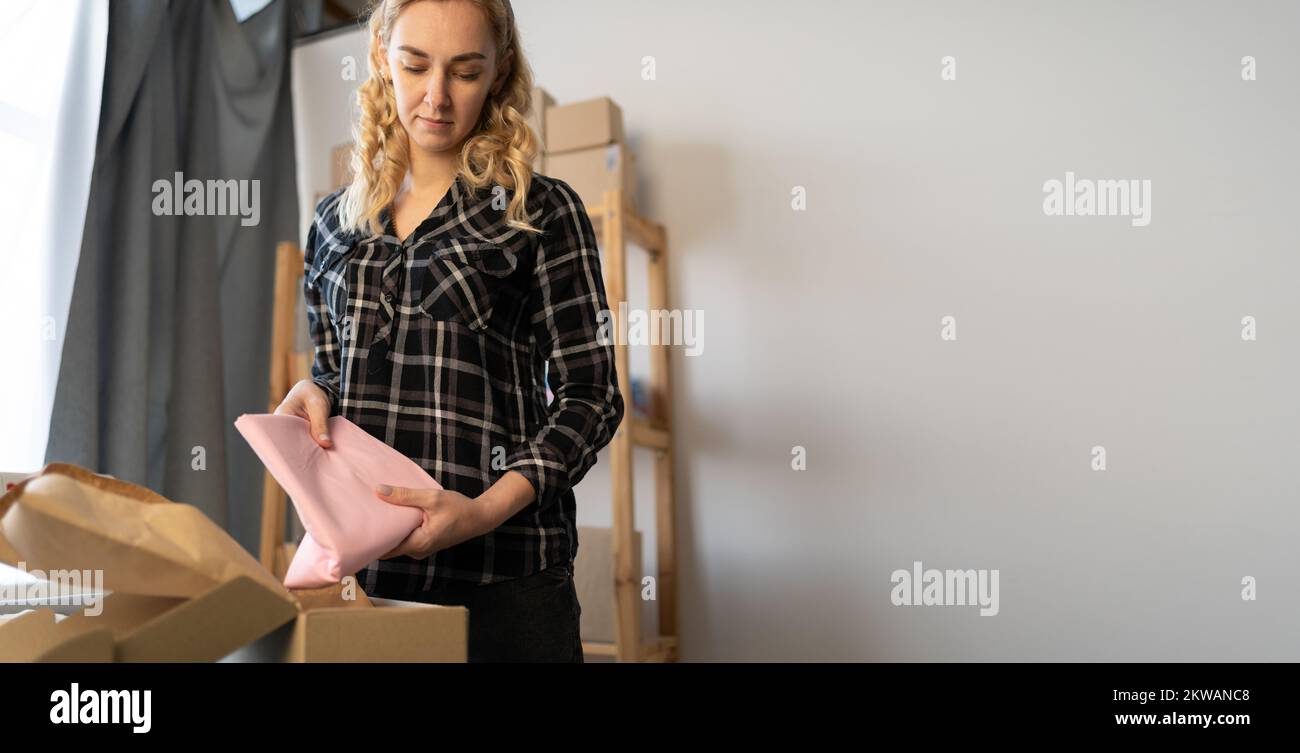 Young woman fashion designer packing of clothes put on the boxes to be ...