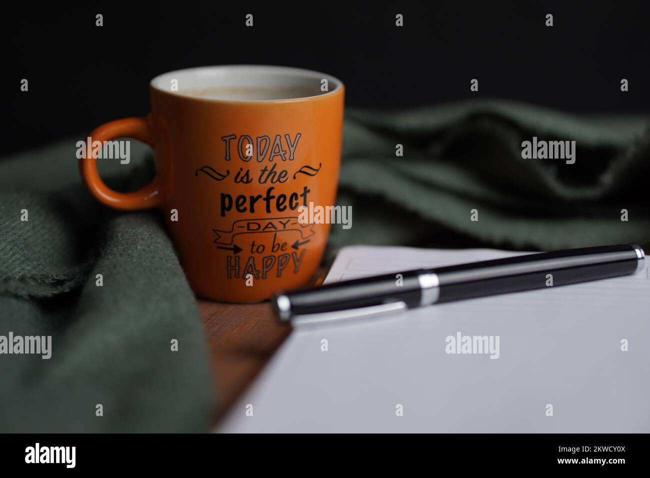 A Cup of hot orange coffee with warm green scarf a on wooden table ...