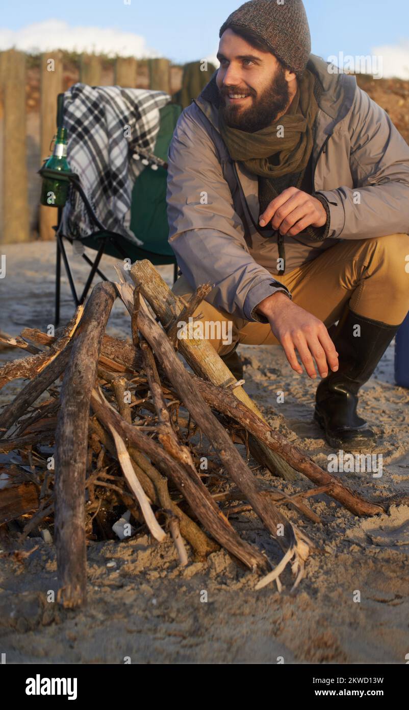 Camping out on the beach. A young man building a fire on the beach ...