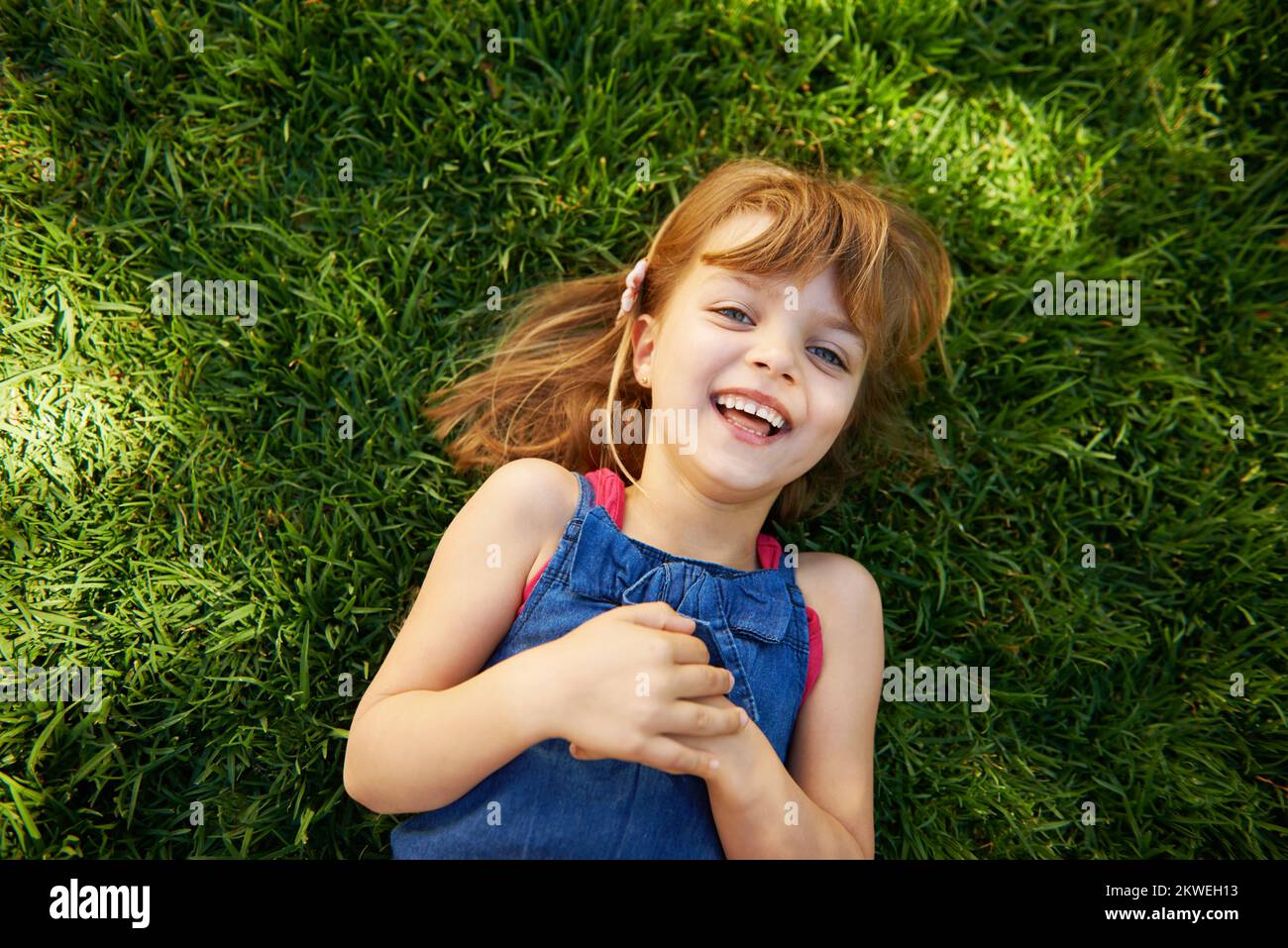 Sunny day fun. a cute little girl smiling while lying down on grass ...